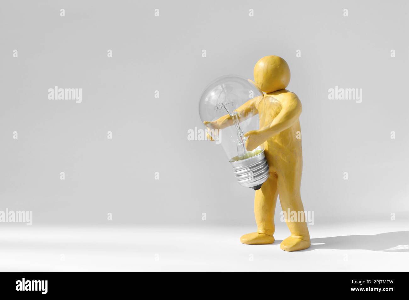 Human figure made of plasticine holding light bulb on white background ...