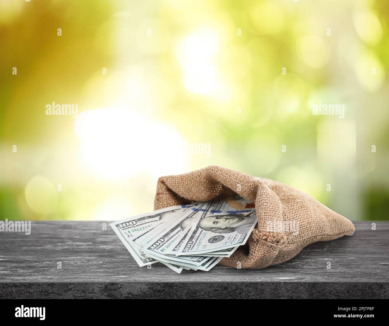 Burlap bag with dollar banknotes on grey stone table against blurred ...