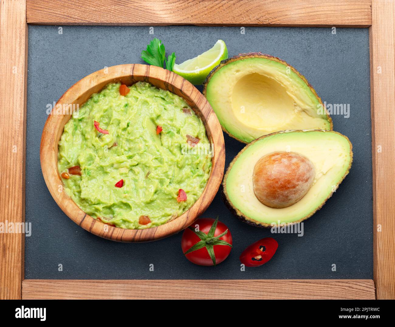 Guacamole and cross section of avocado fruit on gray slate stone board ...