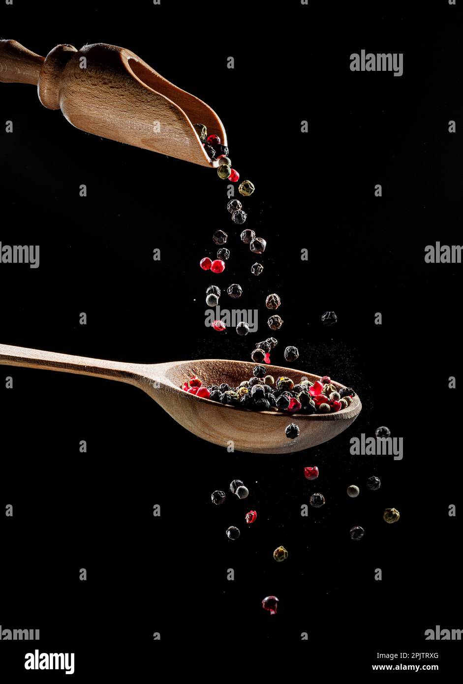 Red and black peppercorns falling down into the wooden spoon at black ...