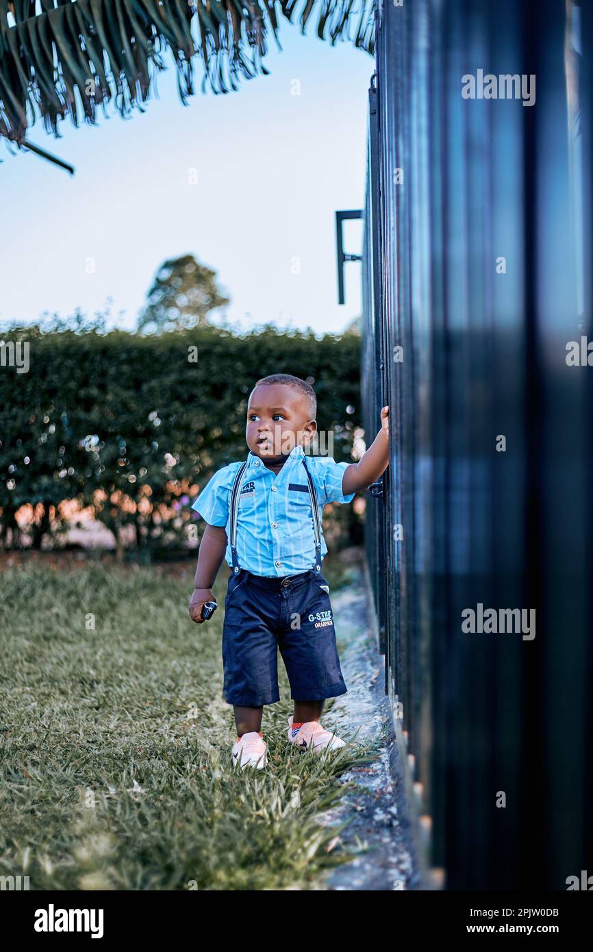 A young Ugandan baby boy in a blue shirt near a fence Stock Photo - Alamy