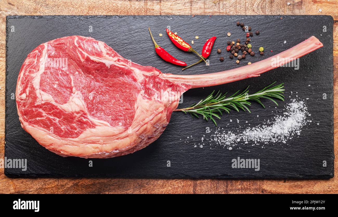 Raw rib steak with bone or tomahawk steak with seasonings on slate ...