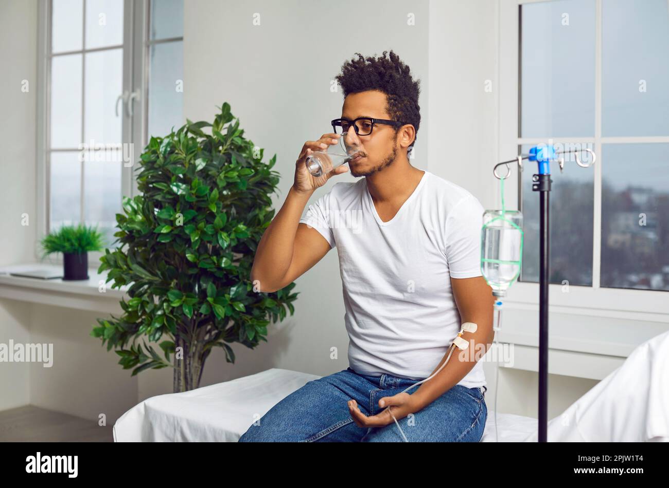 Young man drinks water while receiving vitamin therapy through IV drip ...