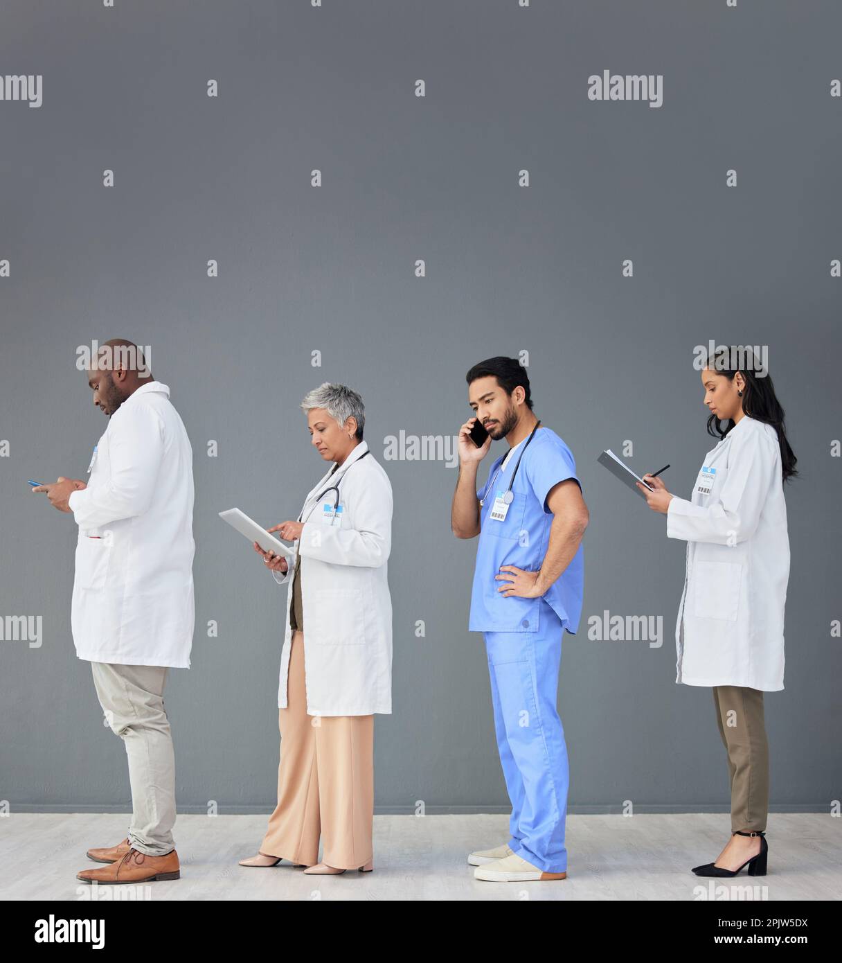 Doctors standing in a row isolated on wall background with tablet ...