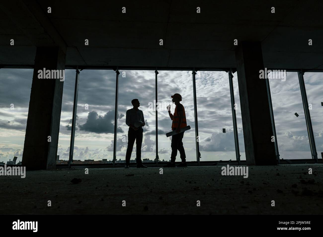 Standing against big window. Man in suit and handyman in orange ...