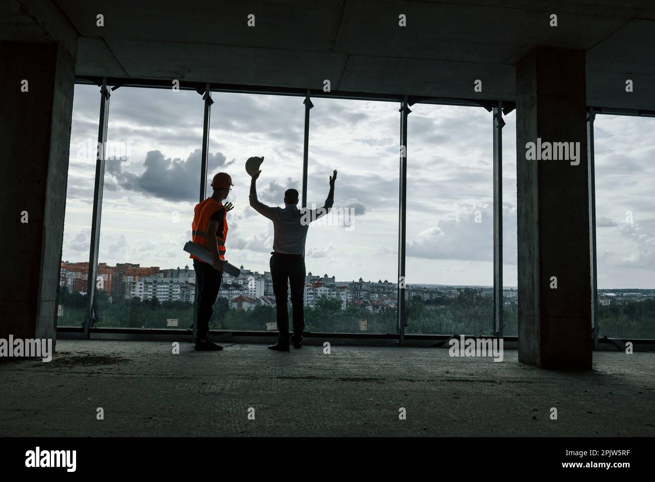 Standing against big window. Man in suit and handyman in orange ...