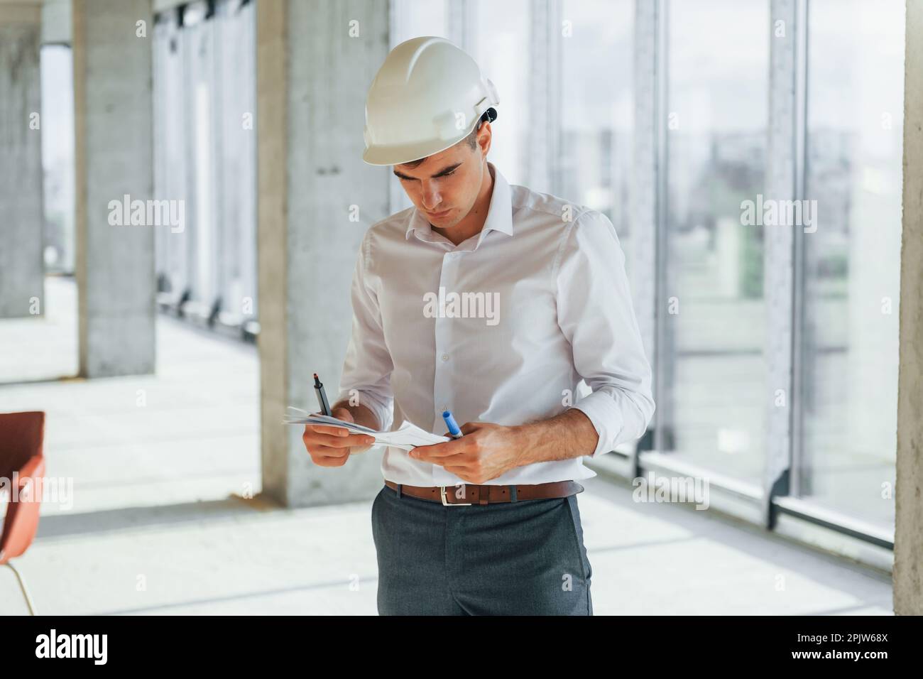 Holds documents. Young man in formal wear is working indoors on the ...