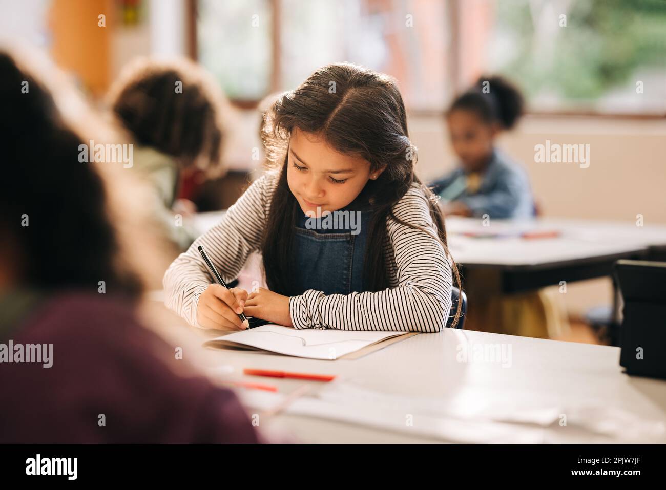 Kid writes on a book in a primary school class. Little girl attending a ...