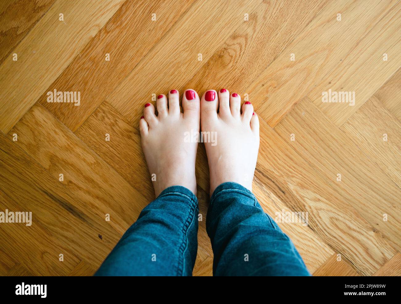 View Of Womans Barefoot Legs Wearing Blue Jeans On Wooden Floor With