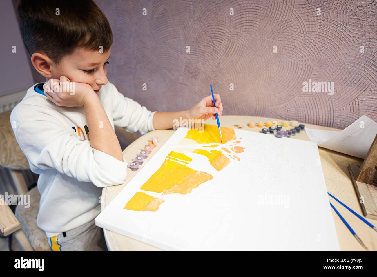 Left handed boy is painting by numbers with gouache at home Stock Photo ...