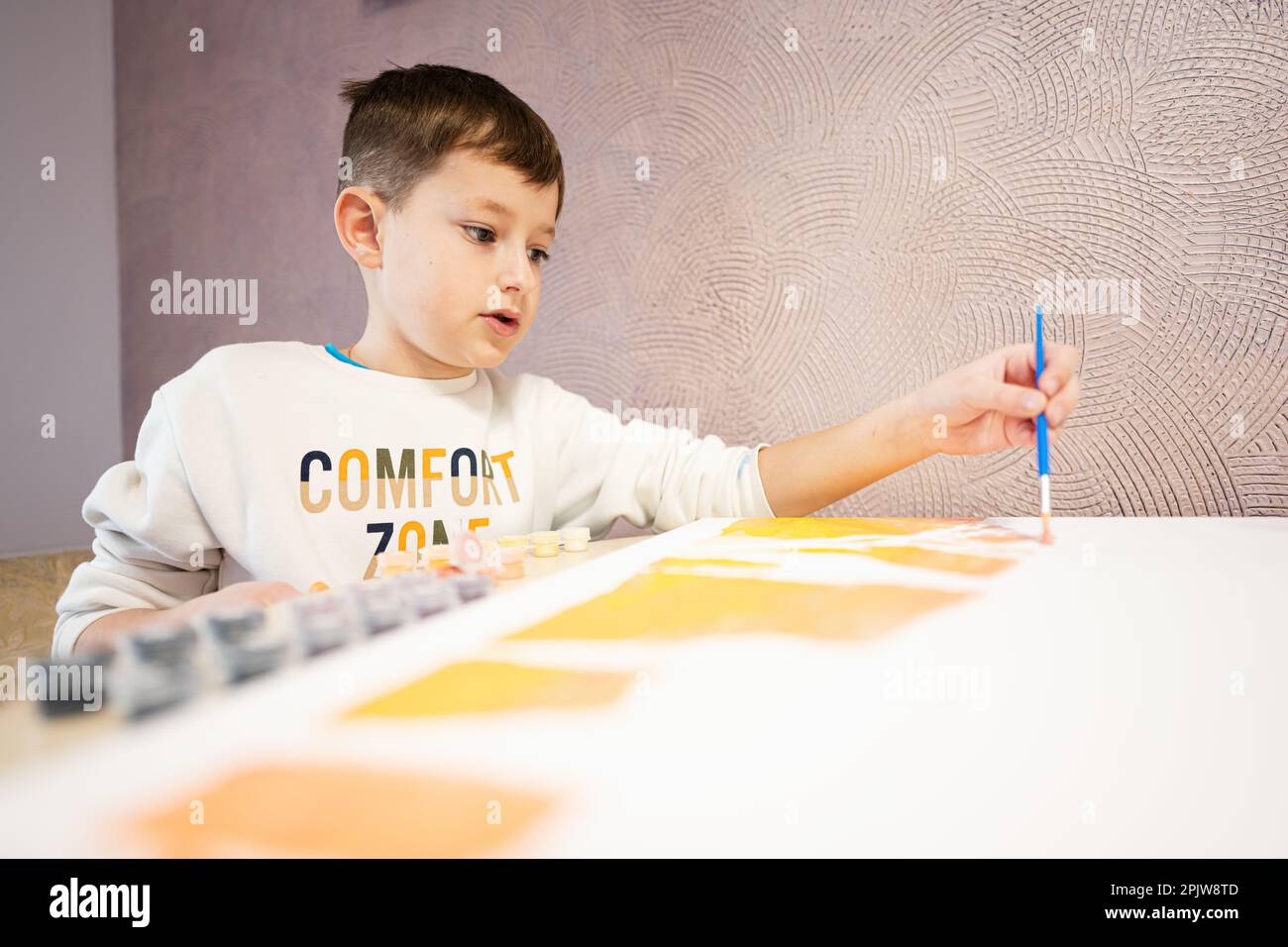 Left handed boy is painting by numbers with gouache at home. Comfort ...