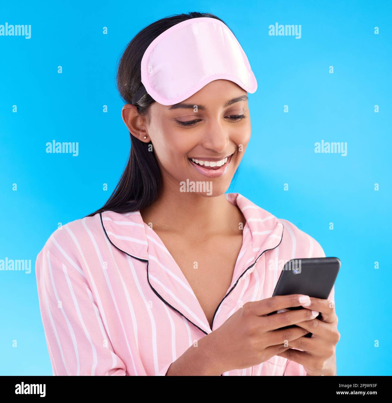 Happy, bedtime and a woman typing on a phone isolated on a blue ...