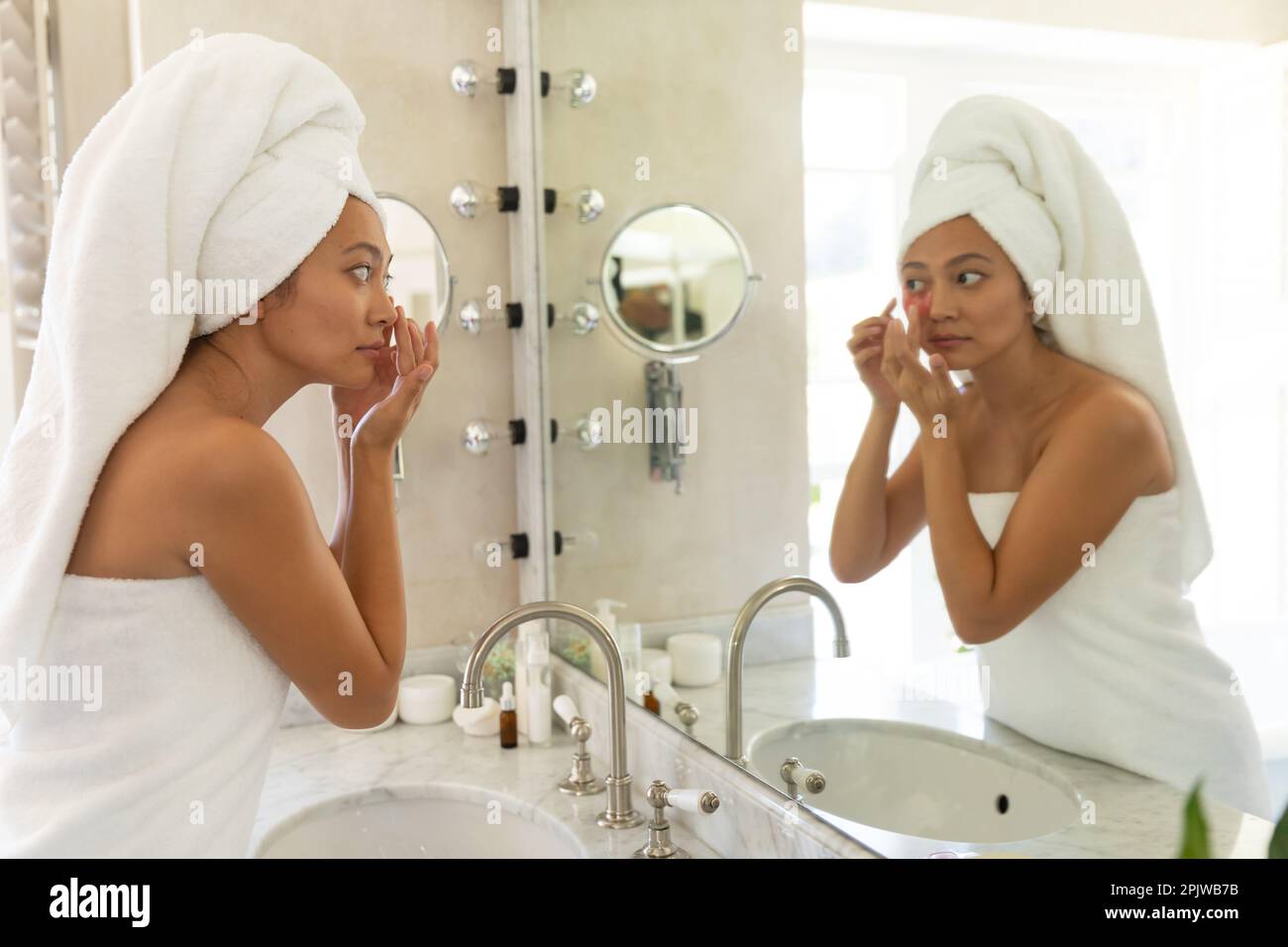Happy asian woman wearing towel on head looking in bathroom mirror ...