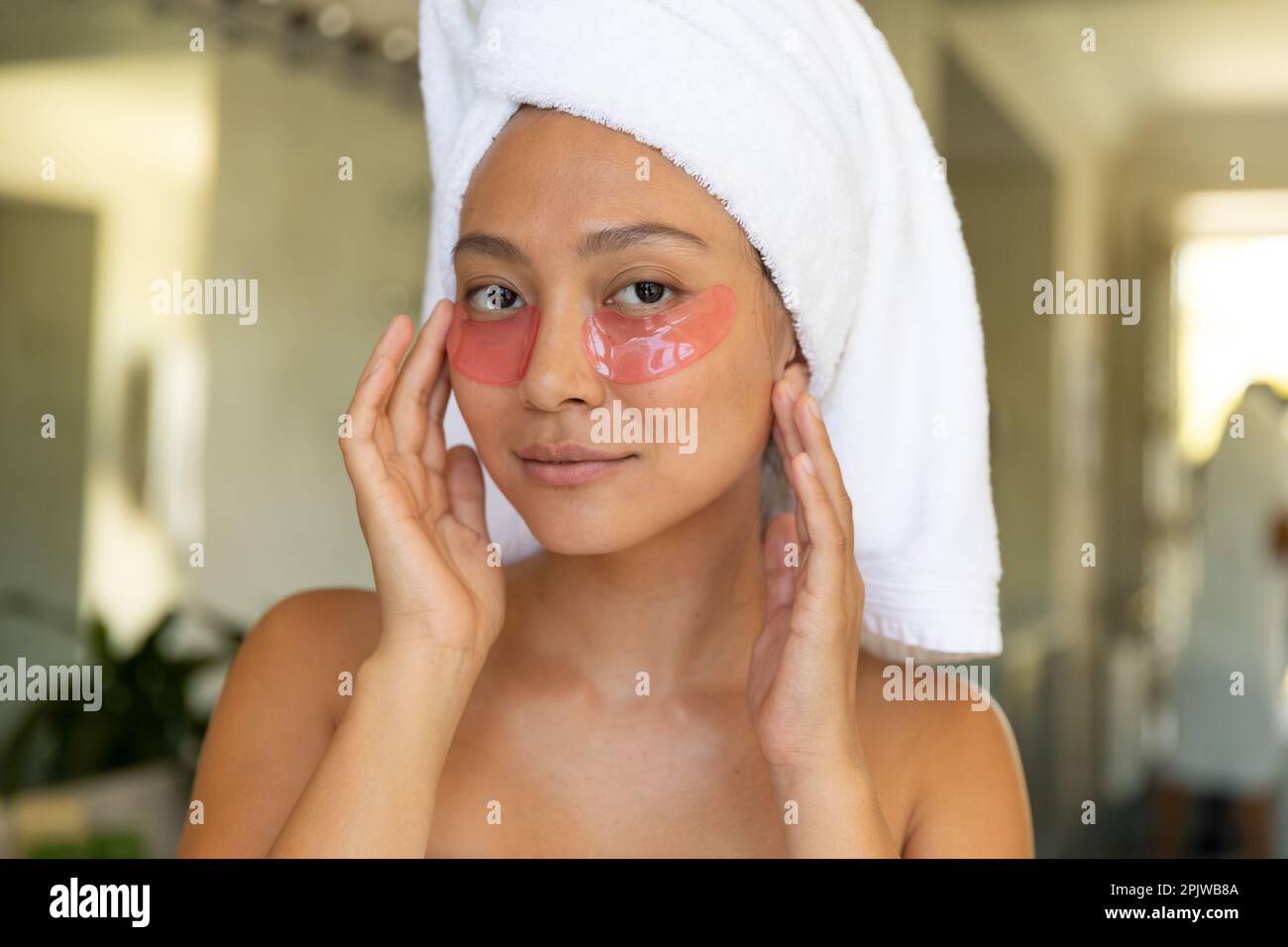 Happy asian woman wearing towel on head looking in bathroom mirror ...