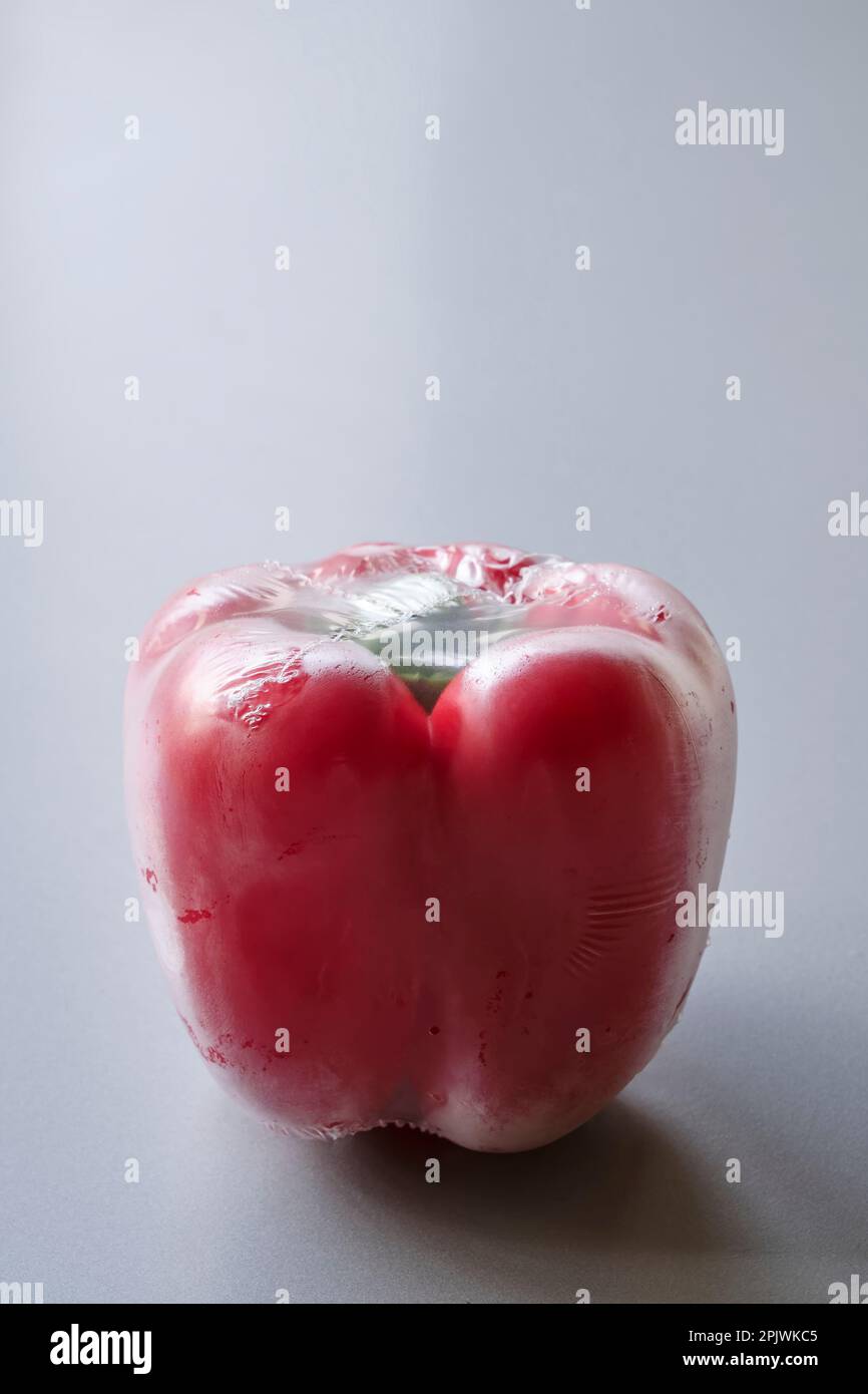Red bell pepper sealed in plastic wrap on a grey background. Dramatic ...