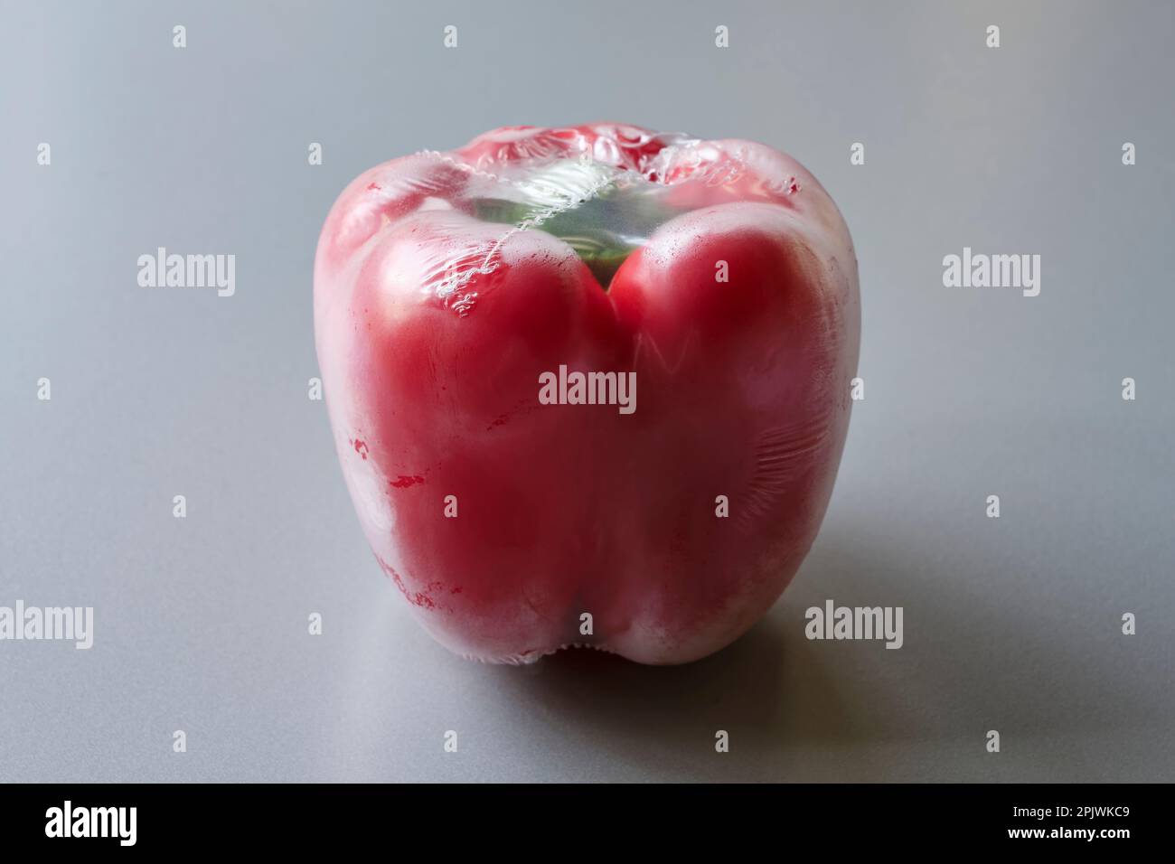 Red bell pepper sealed in plastic wrap on a grey background. Dramatic ...