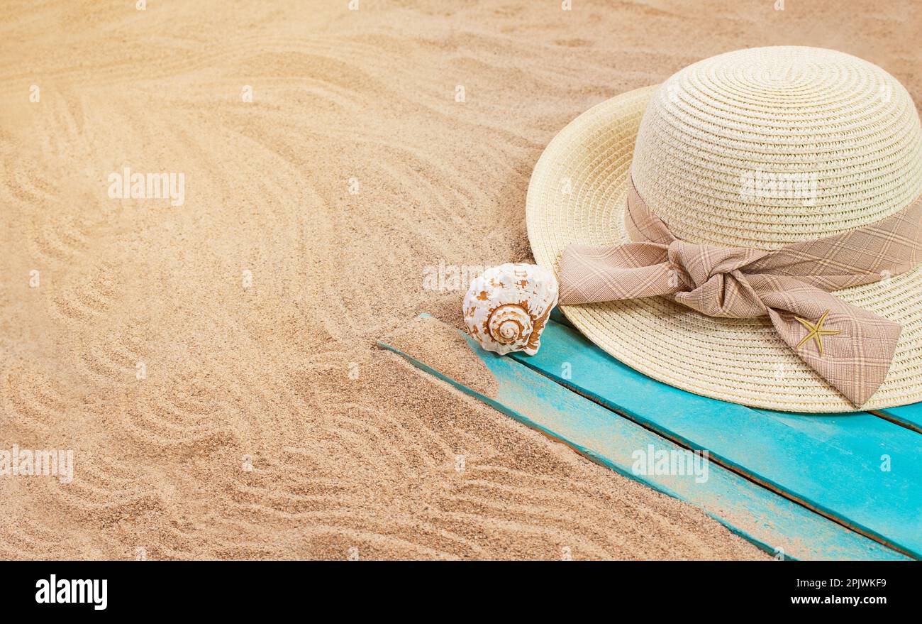 Sun hat with seashell and starfish on blue wooden board on sandy beach ...