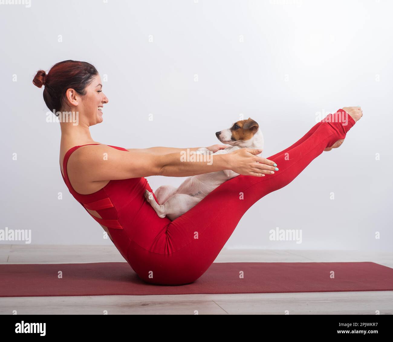 A woman in a red overalls practices yoga with a dog. The girl performs ...
