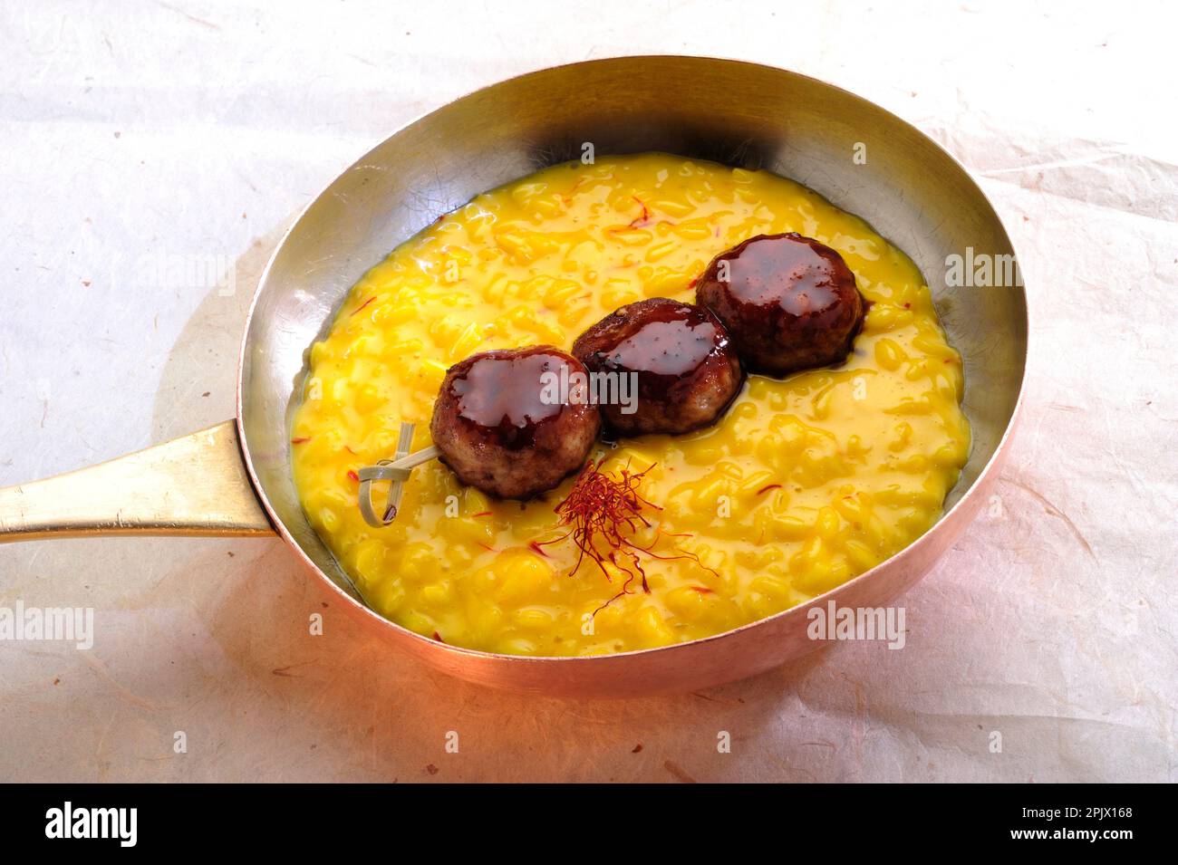 A saffron risotto dish with a meat balls skewer in a copper pan Stock ...