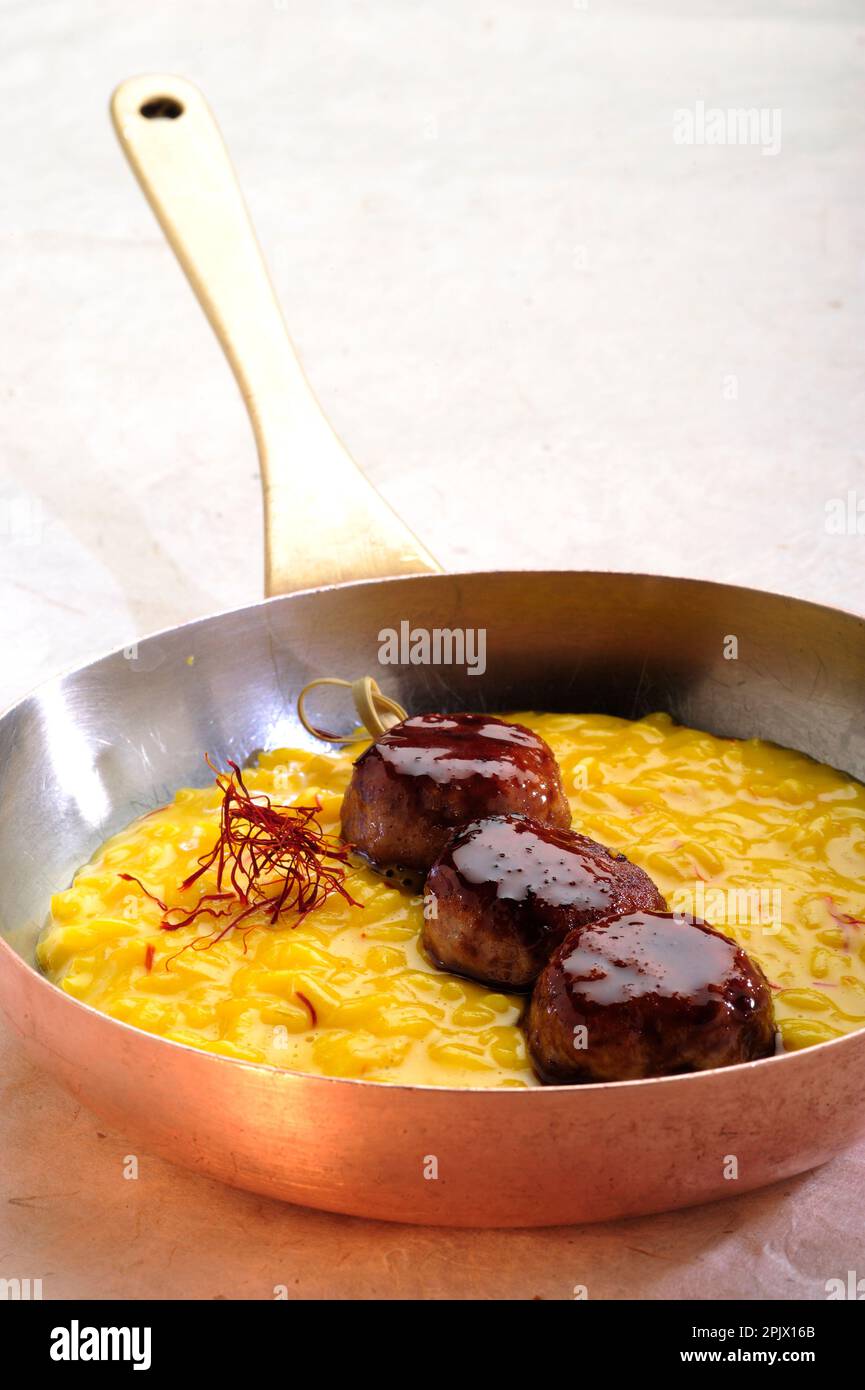 A saffron risotto dish with a meat balls skewer in a copper pan Stock ...