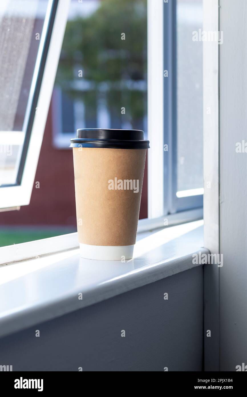 Disposable brown and white coffee cup with black cap on a window sill ...