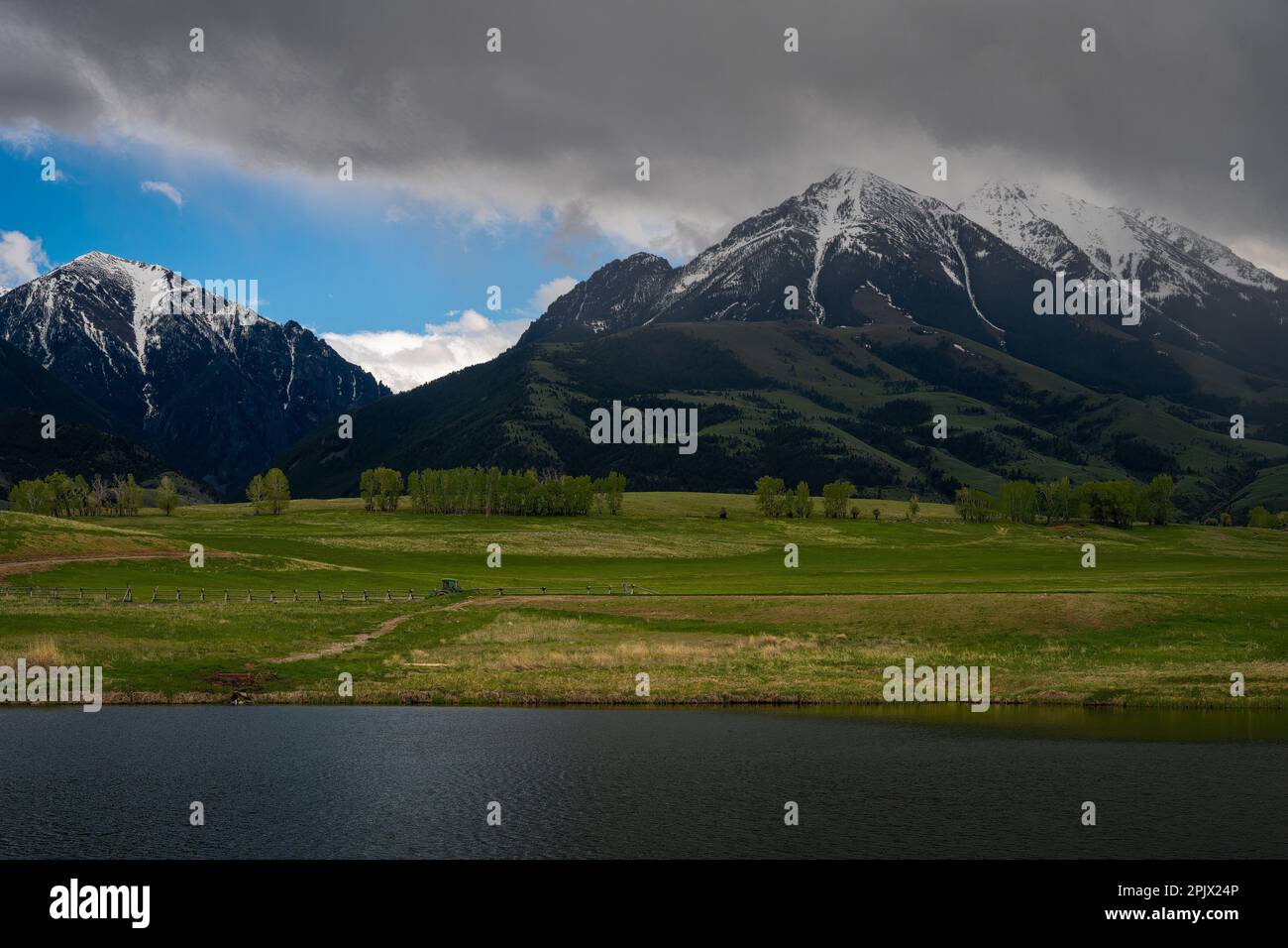 The snow capped Absaroka mountains with a lush green field and lake ...
