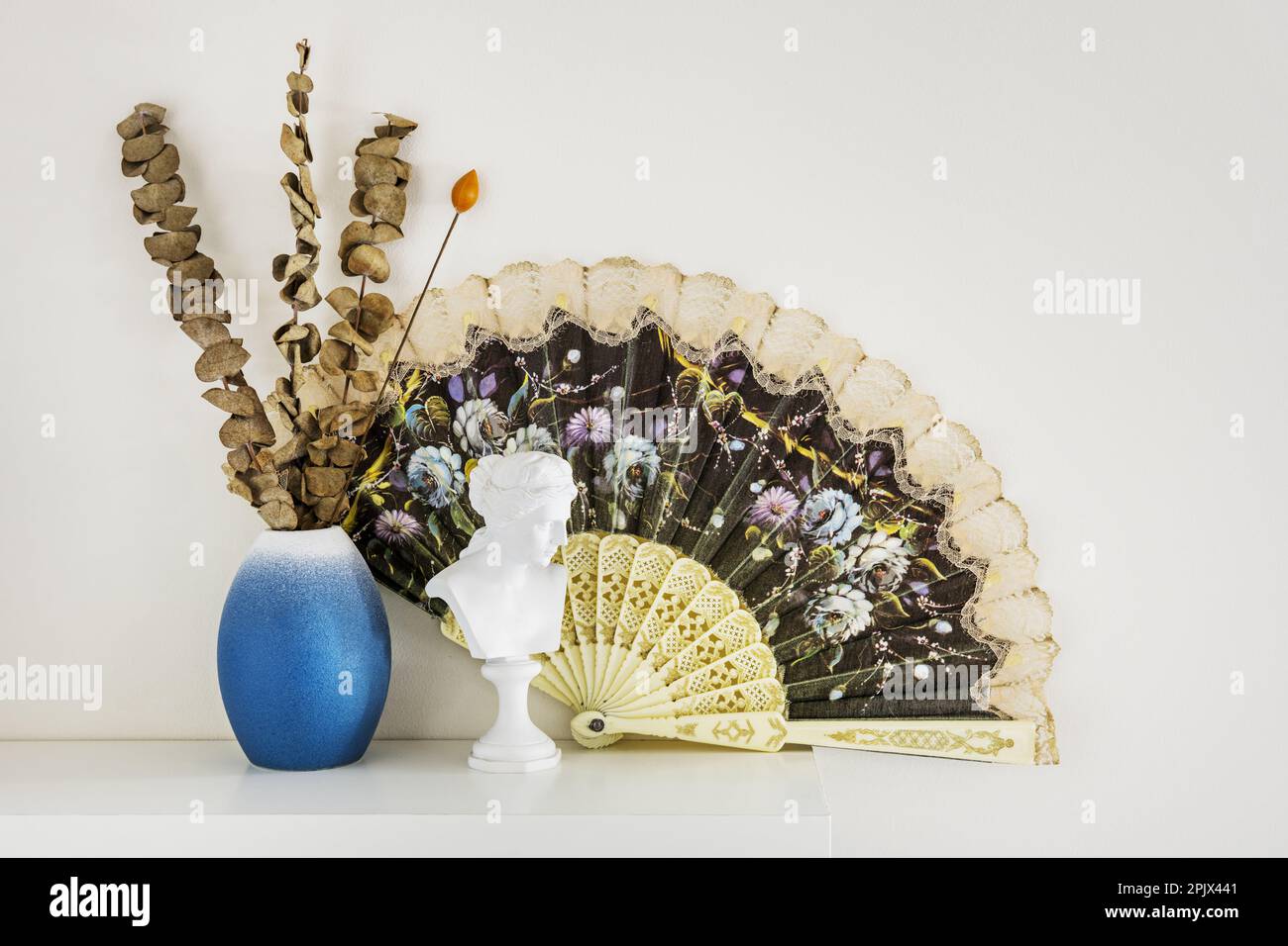 Decorative objects and a fan that are located on a white wall shelf ...