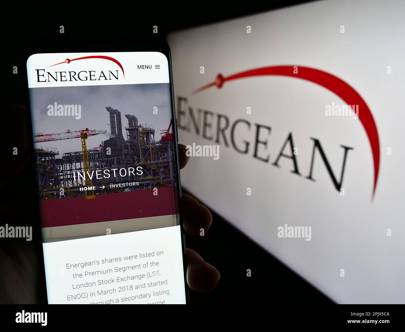 Person holding mobile phone with website of British oil and gas company Energean plc on screen ...