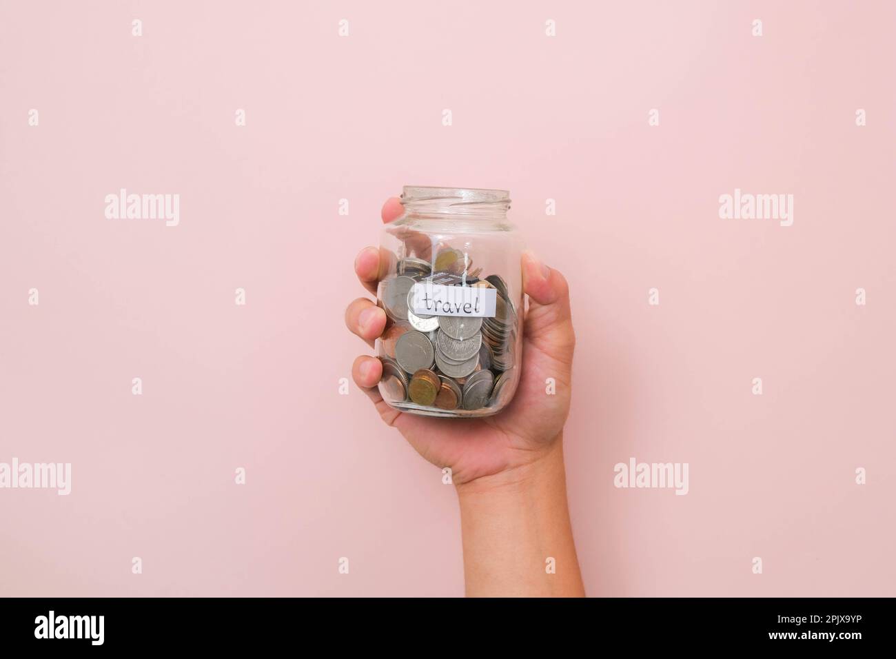 Close-up of hand holding glass jar with money (coins) inside on pink ...