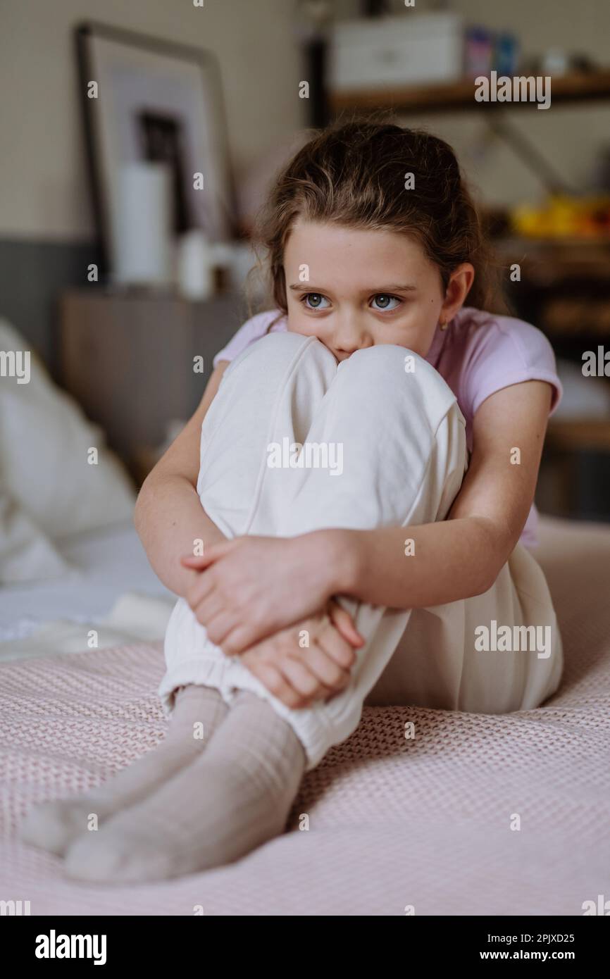 Little sad girl sitting alone on a bed Stock Photo - Alamy