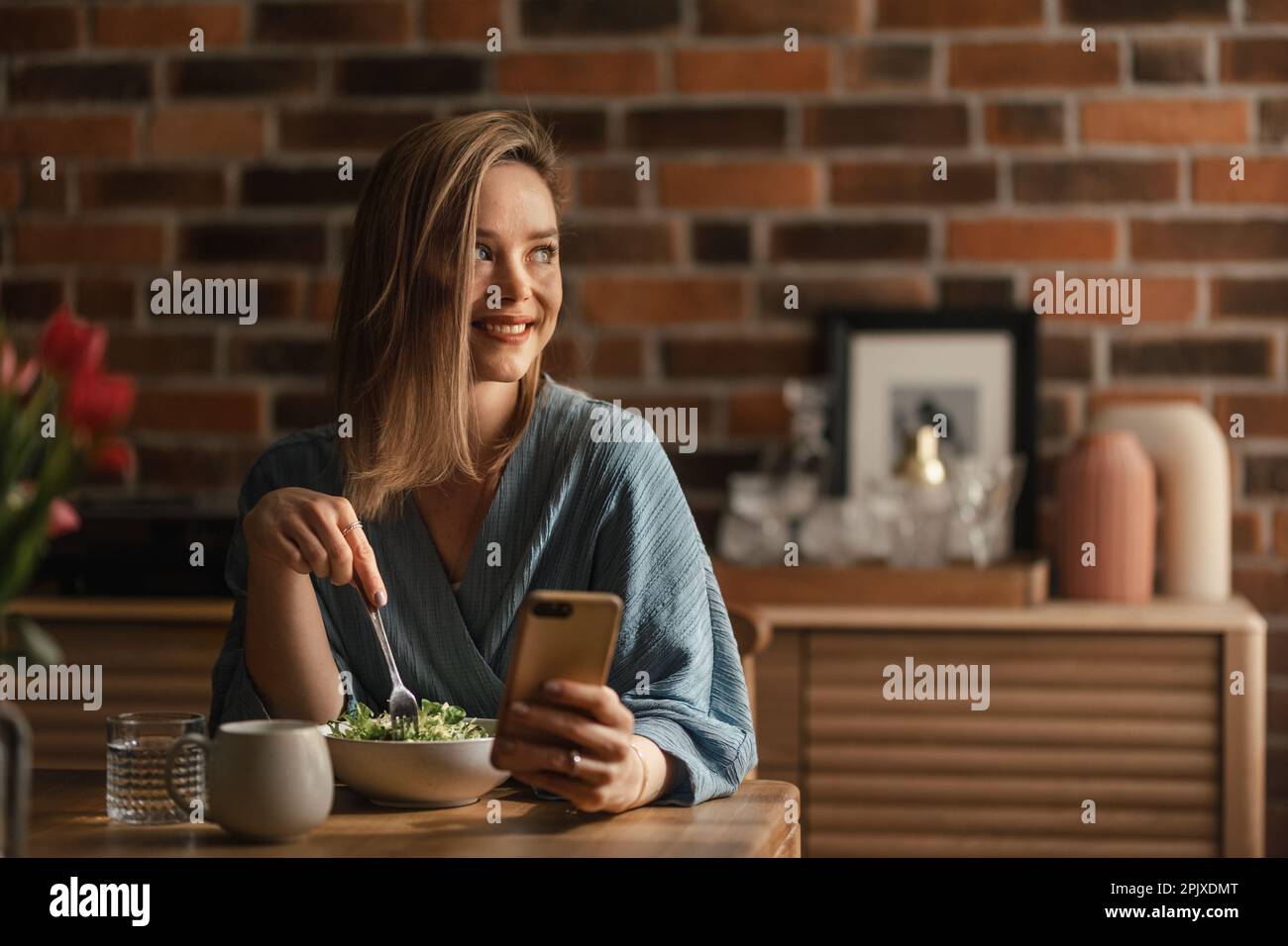 Young woman eating salad and scrolling her phone Stock Photo - Alamy