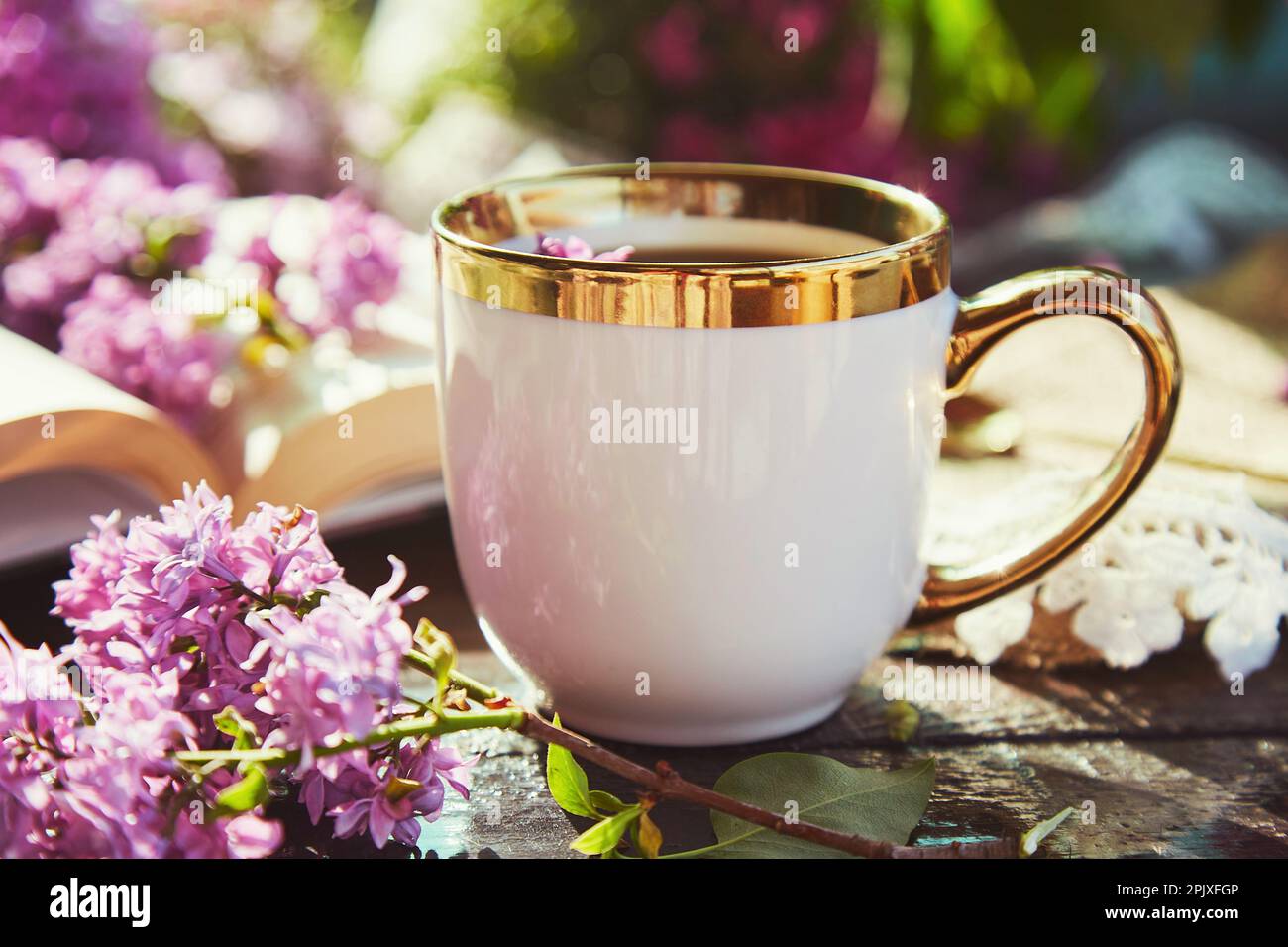 Coffee break with cup of coffee among lilac flowers. Reading a book ...