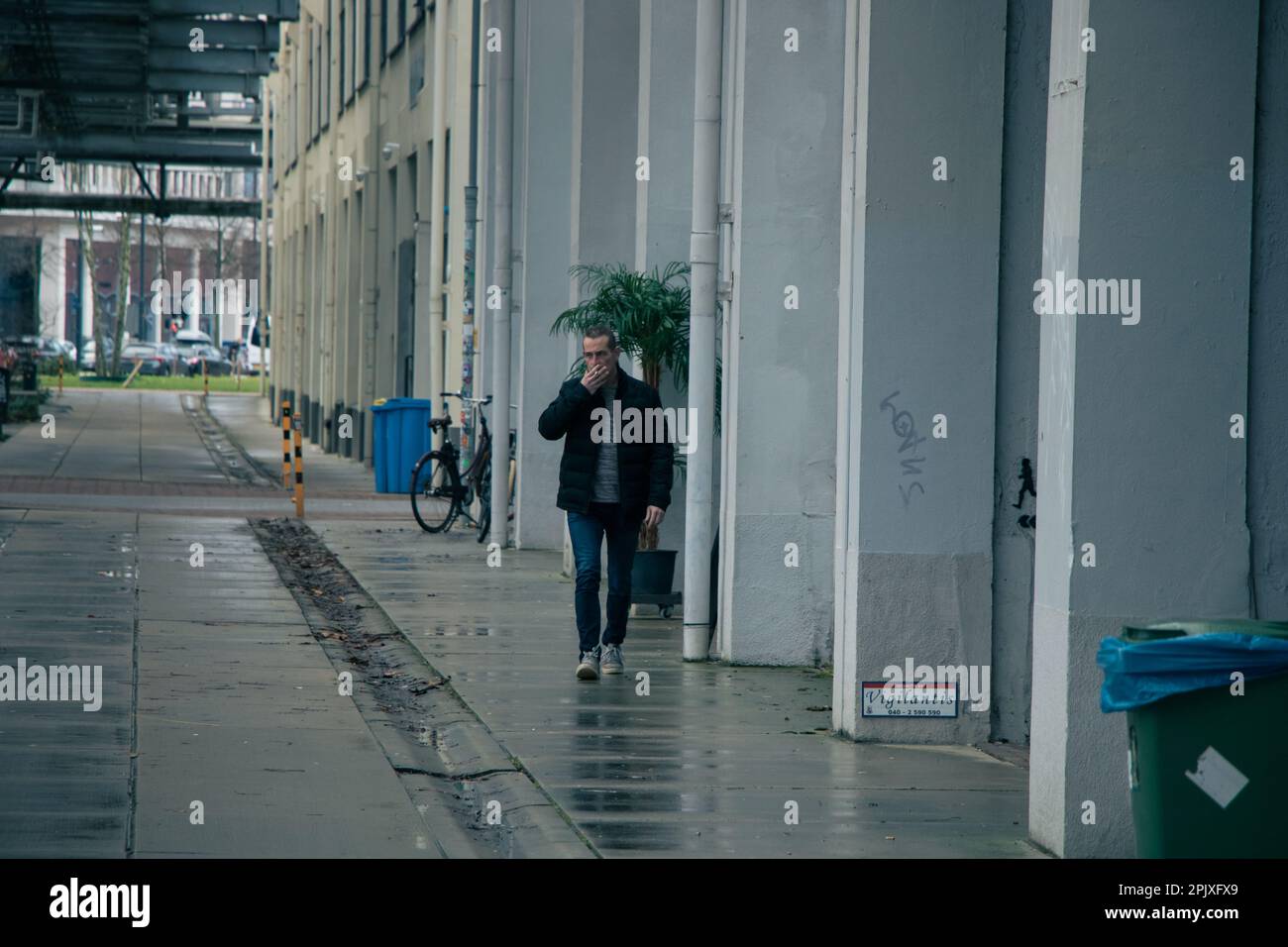 A man smoking a cigarette on a rainy day, walking down the Strijp-S ...