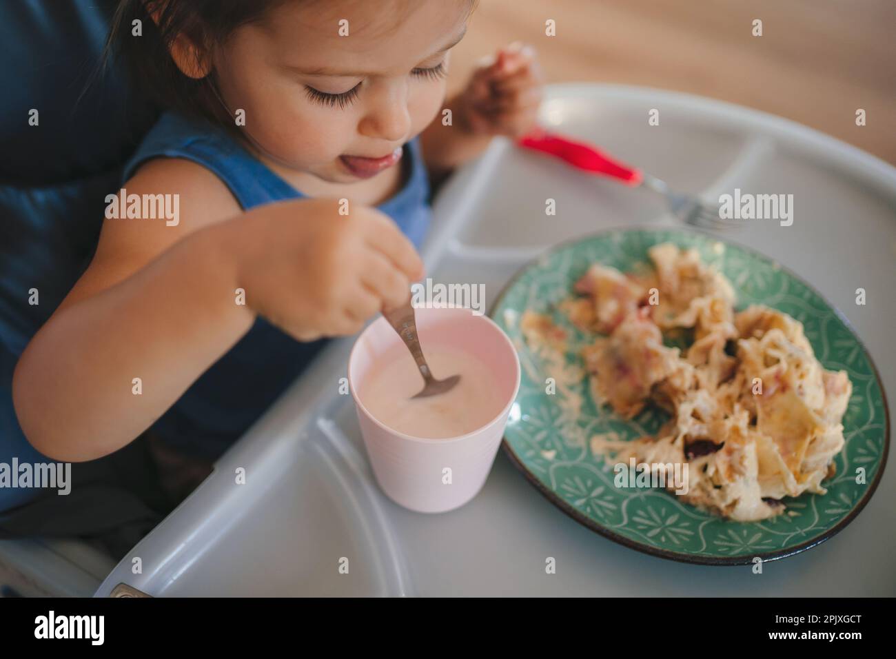 Caucasian baby girl eating lunch from plate sitting high chair, self ...