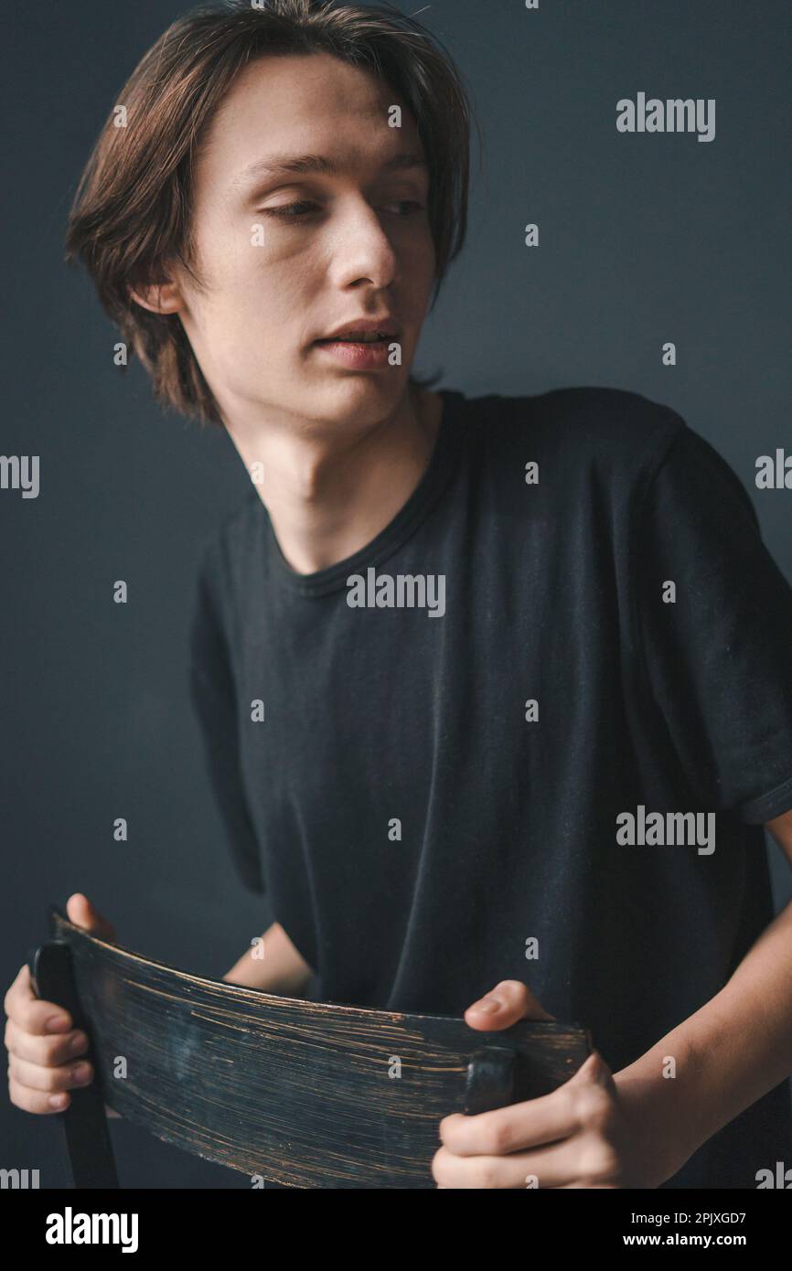 Dreamy relaxed young man wearing unlabeled black t-shirt sitting on a ...