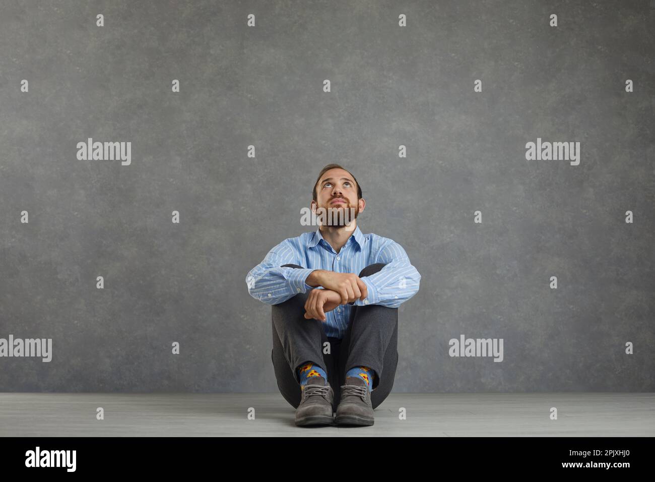 Relaxed man sitting on floor looking up and dreaming at future studio ...