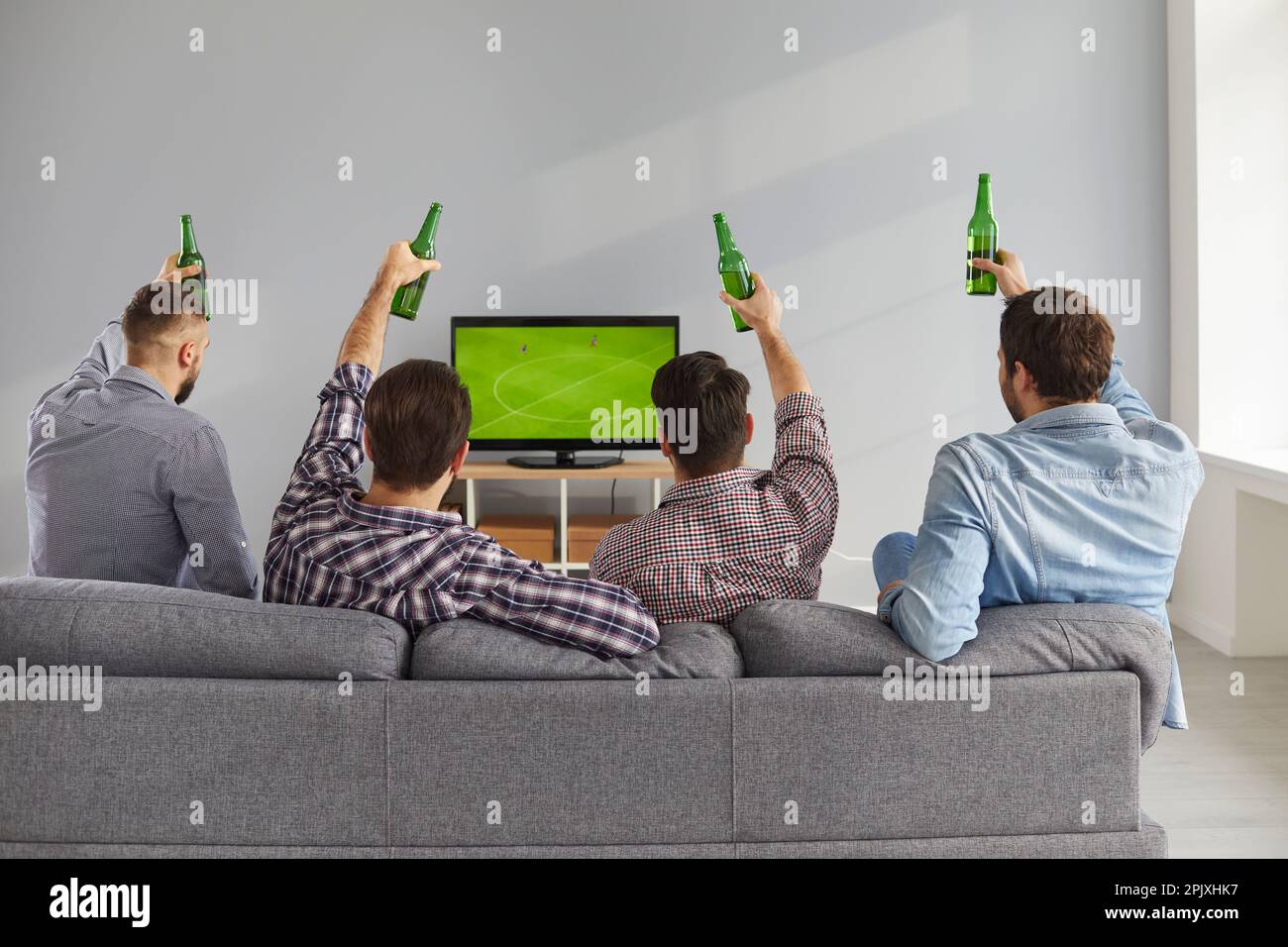 Back view of young men sitting on couch, watching soccer match and ...