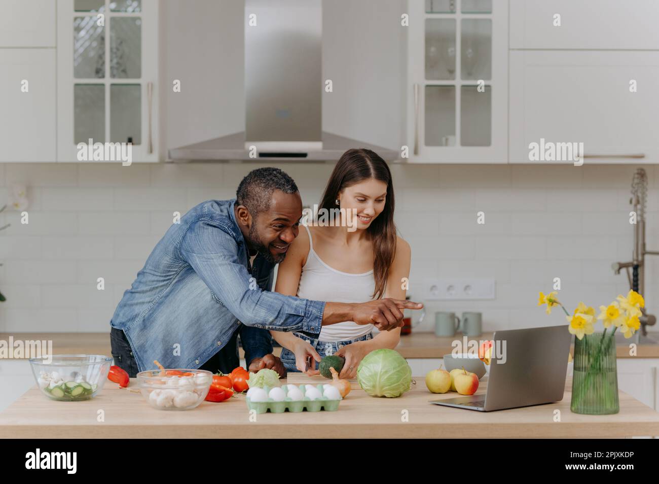 A married couple cooks together using a laptop, searching for recipes ...