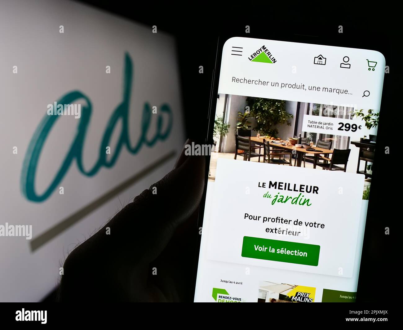Person holding cellphone with webpage of French retail company Adeo S.A ...