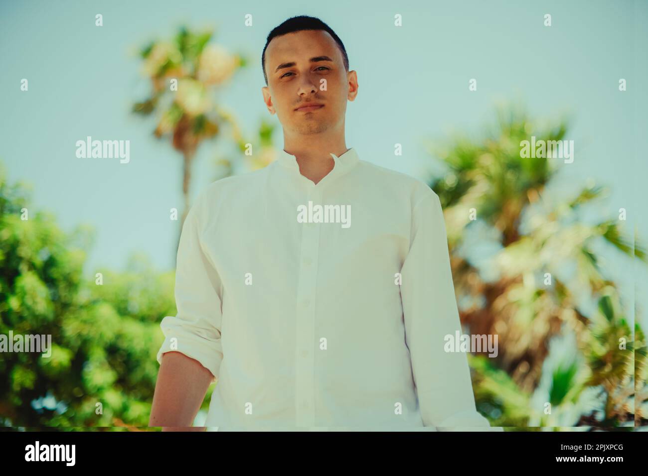 A handsome young man in a white shirt stands against a background of ...