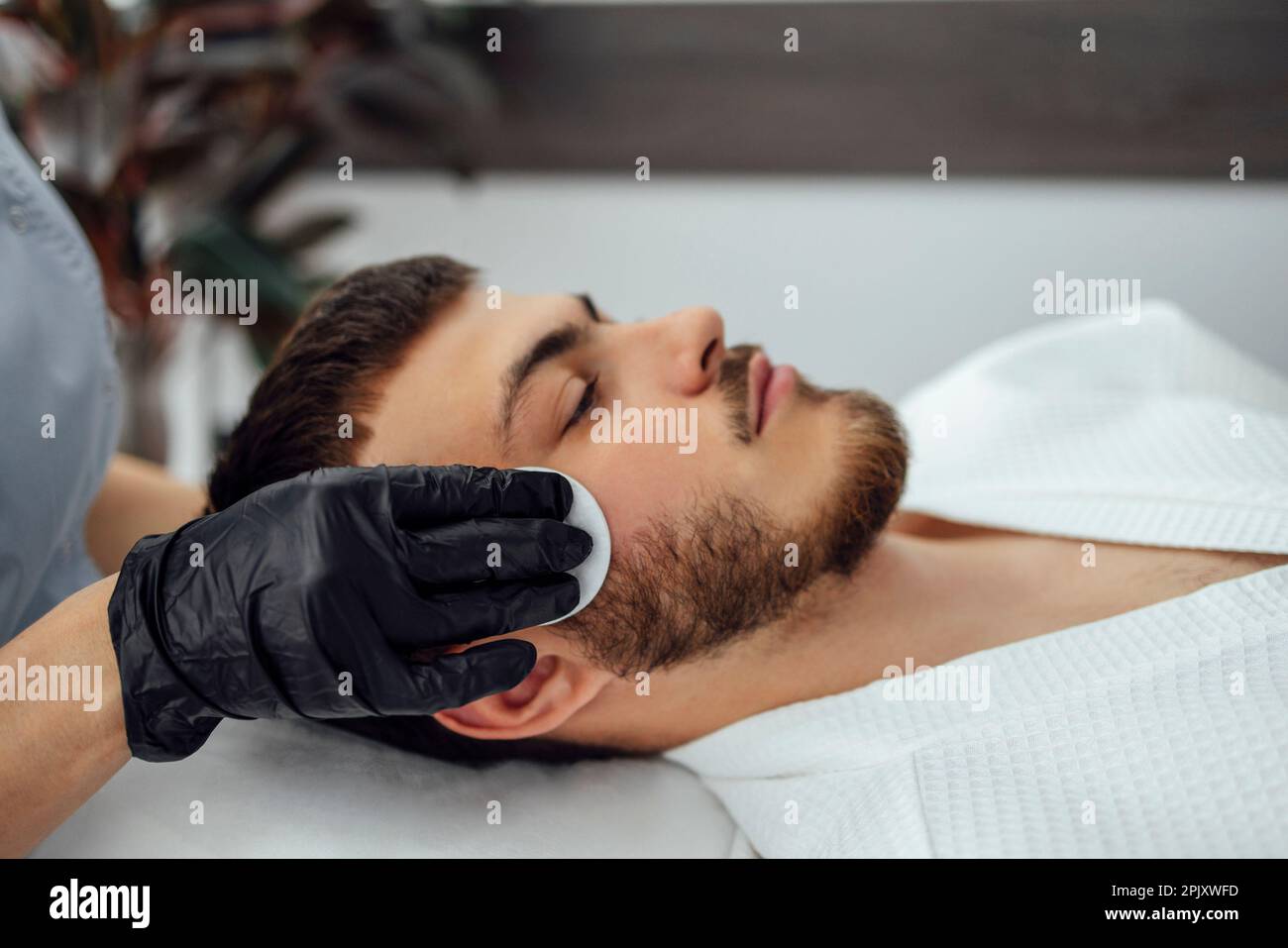 Facial skin cleansing in beauty salon. Beautician in black gloves wipes ...