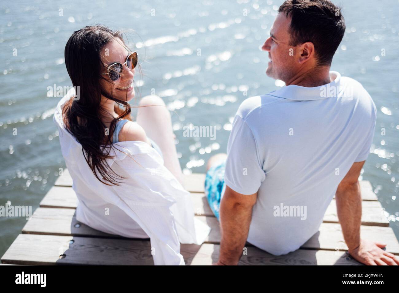 Young couple in love in light casual clothes is sitting on wooden ...