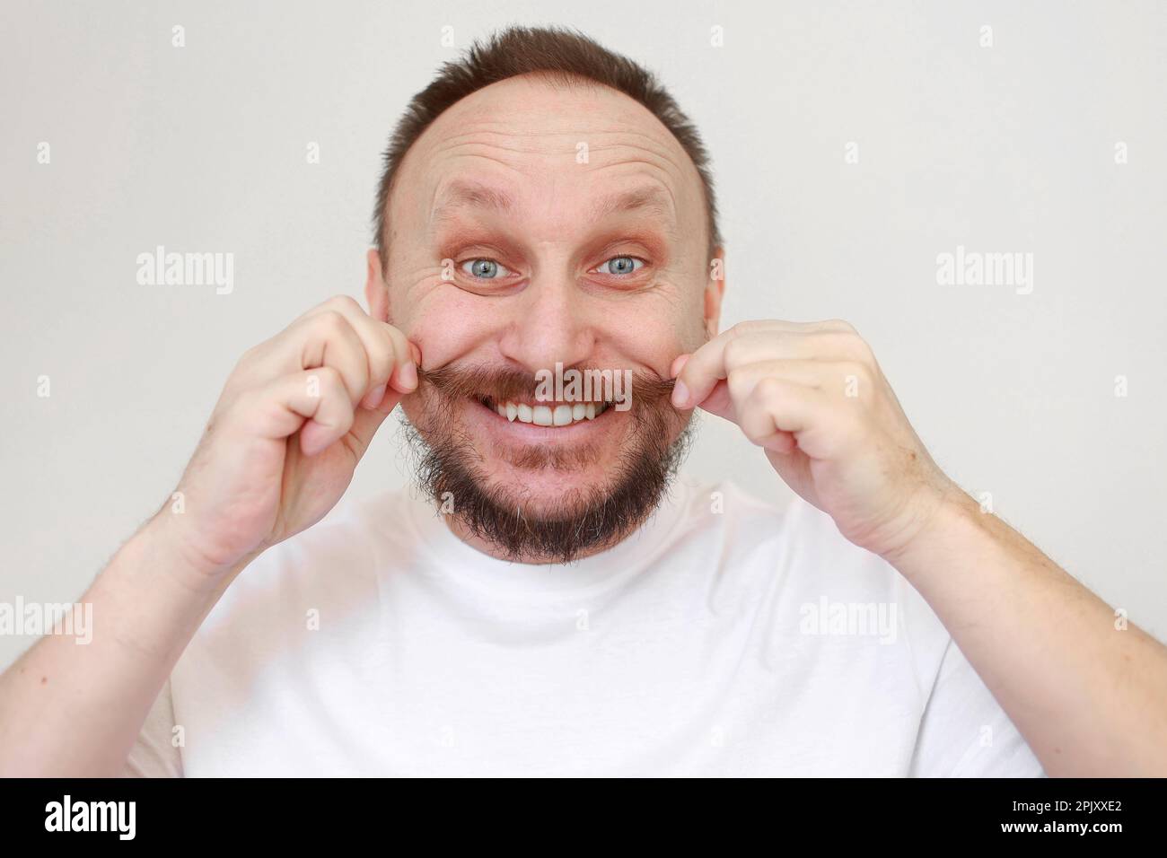 Portrait of happy caucasian bearded man touches his moustache in white ...