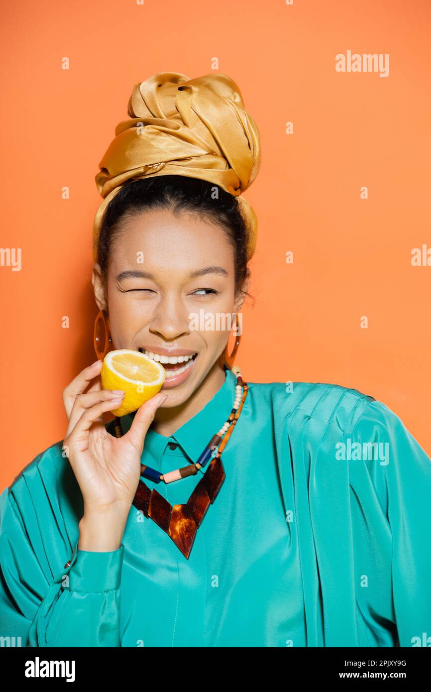 Portrait of stylish african american woman biting lemon on orange ...