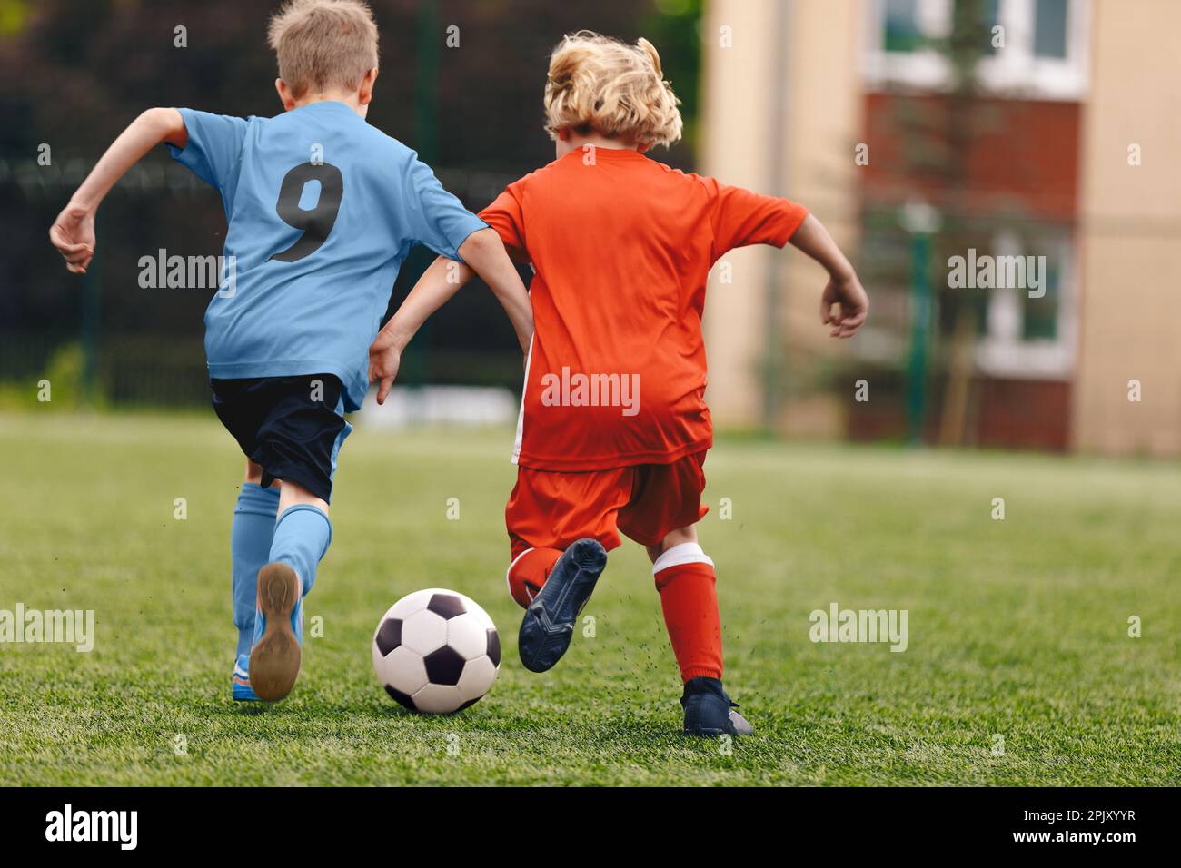 Two school boys kicking a soccer ball. School boys in red and blue ...