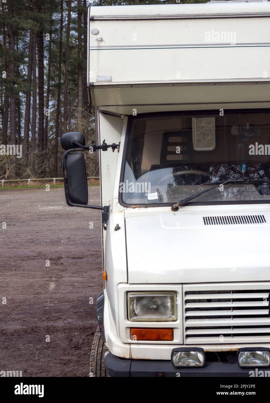 An old camper van parked in a car park surrounded by trees and plants ...