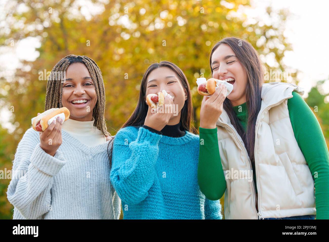 Multiethnic friends joking while eating hot dog in a park Stock Photo ...