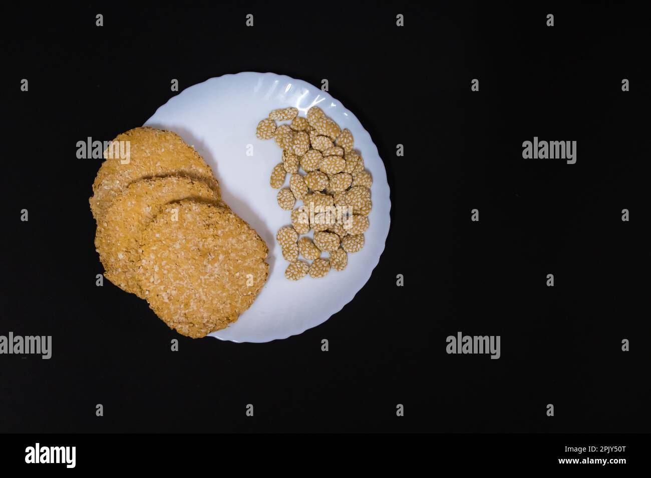 indian traditional sweet tilkut in white plate with black background ...