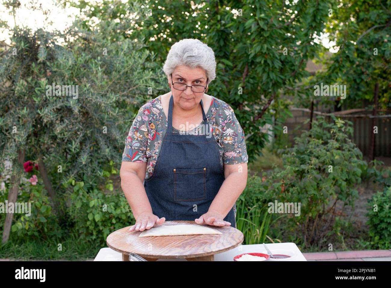 Female cook, chef with grey hair making pita on wooden board outdoor ...