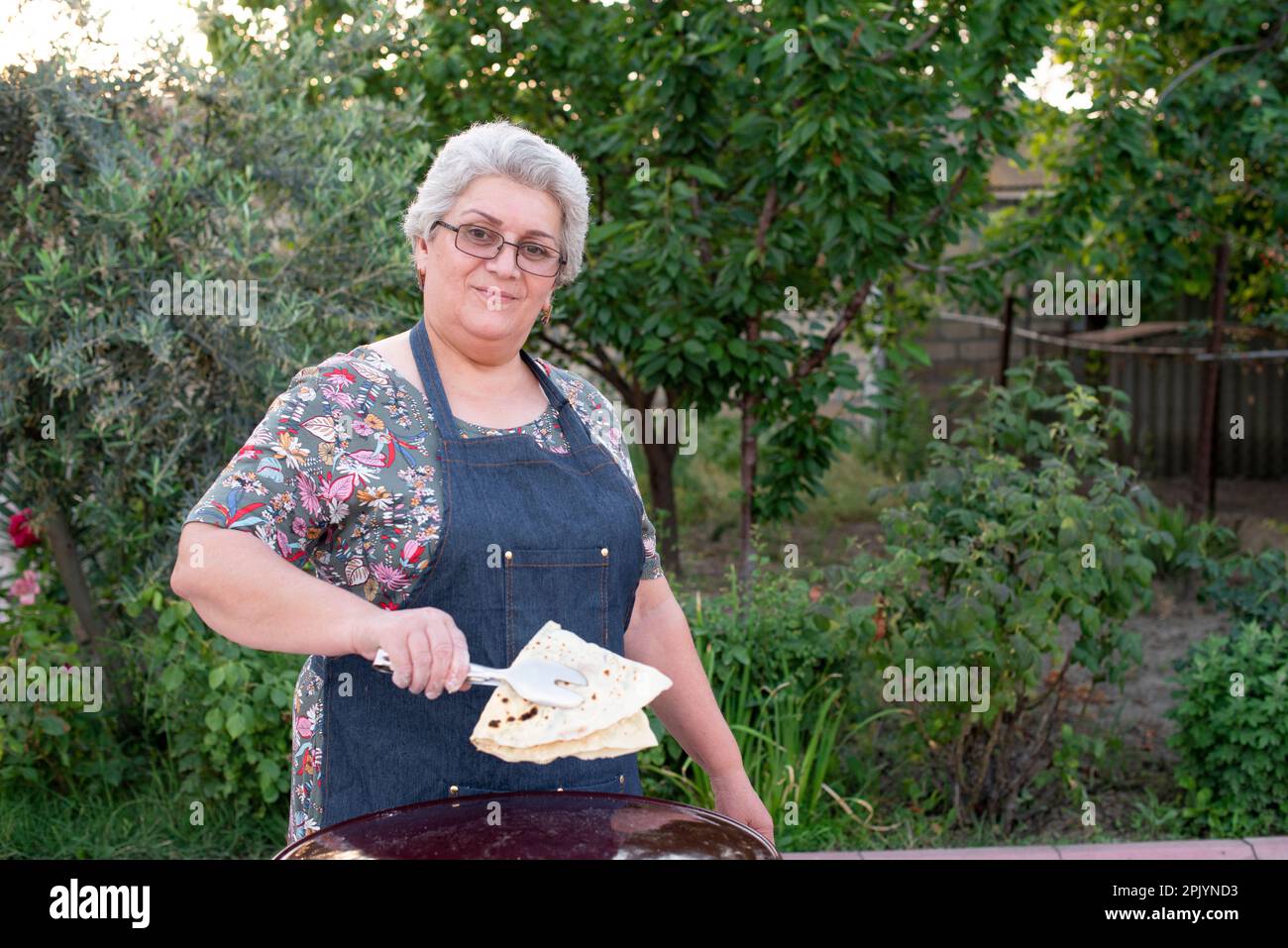 Chef, coock, old woman looking at camera, smiling, frying, cooking pita ...